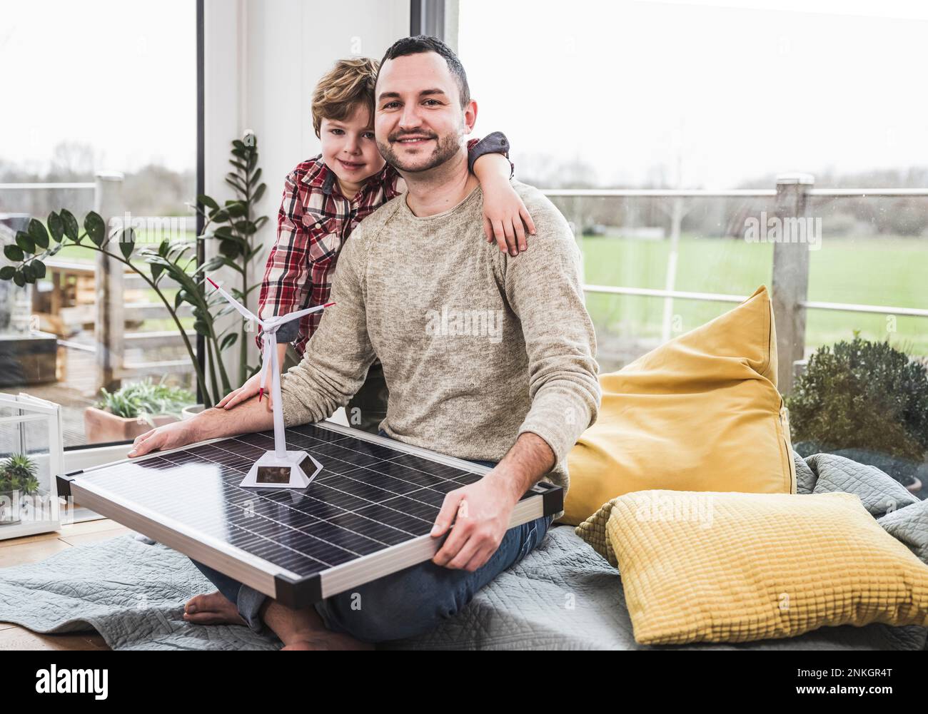 Smiling man with wind turbine and solar panel model by son at home ...