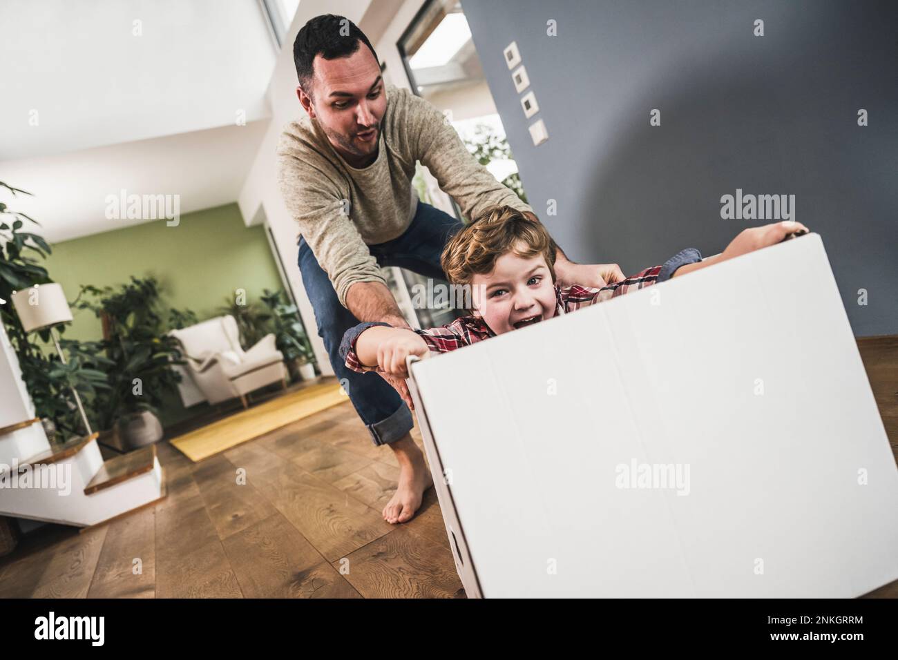 Happy father pushing son sitting in cardboard box at home Stock Photo ...