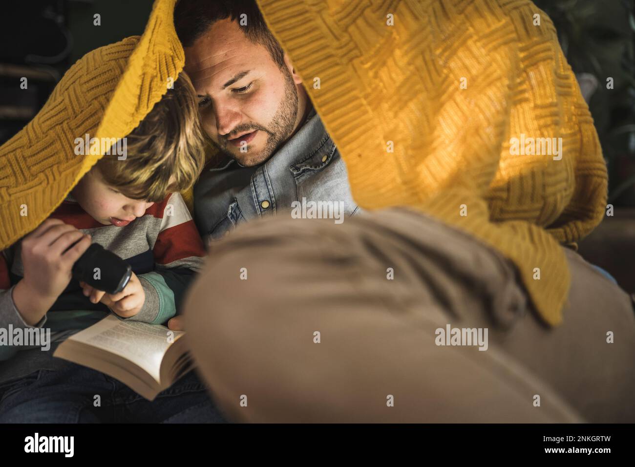 Father and son with torch reading book under yellow blanket Stock Photo ...