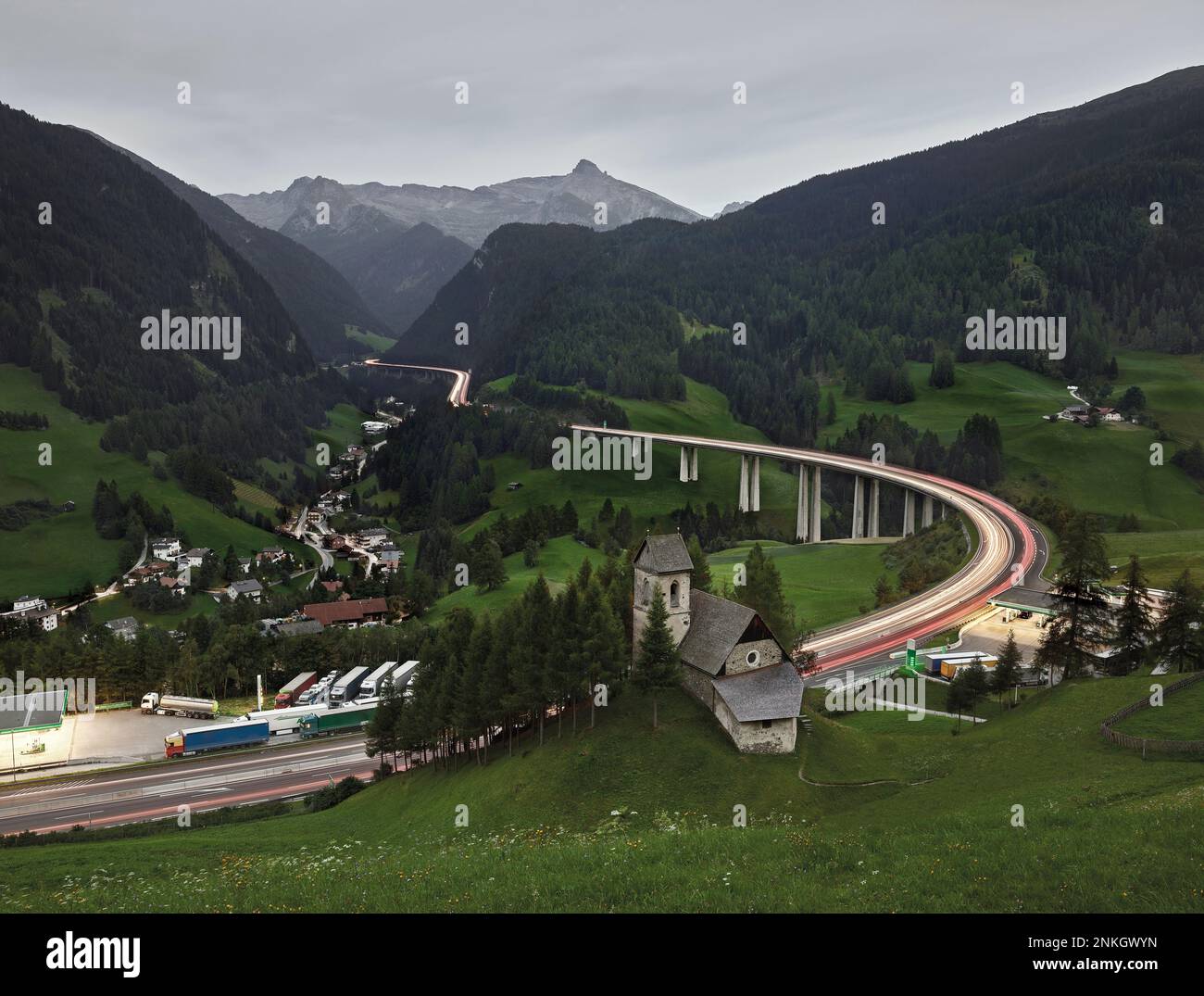 Vehicle light trails along elevated road stretching alpine village hi ...