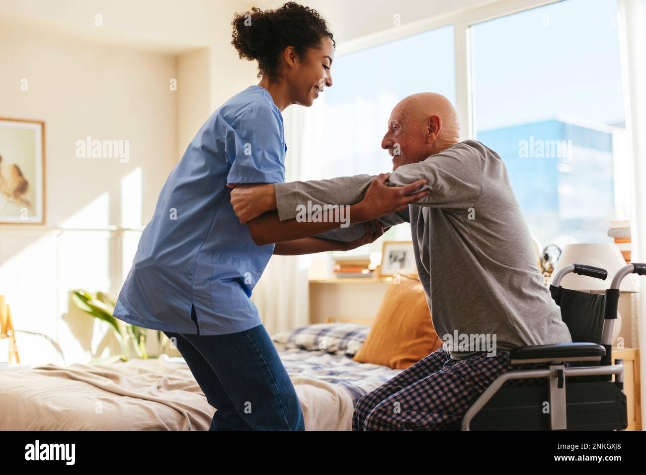 Physical therapist helping senior man in getting up from wheelchair at ...