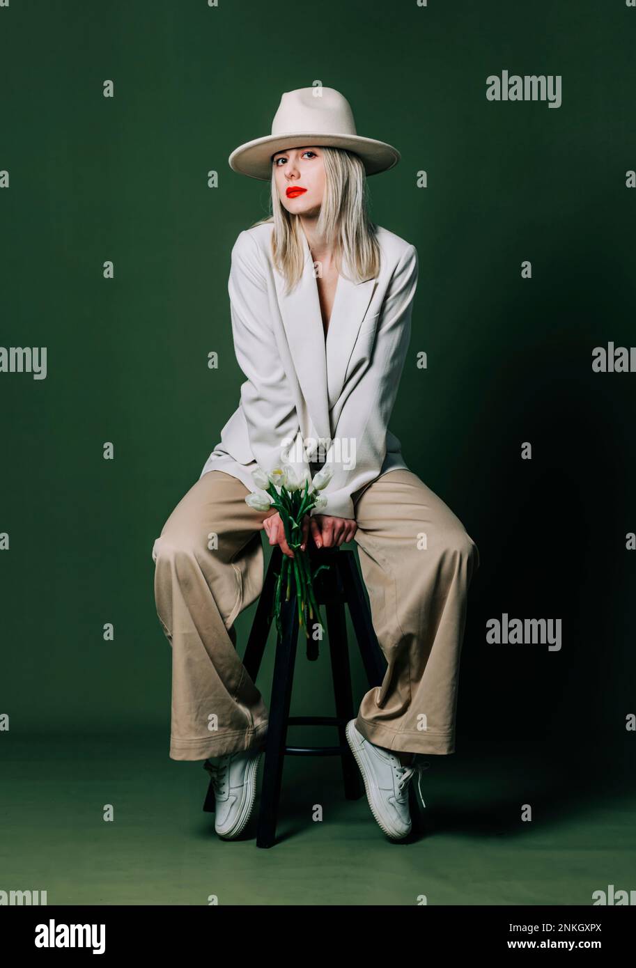 Woman with hat sitting on stool in front of green background Stock ...