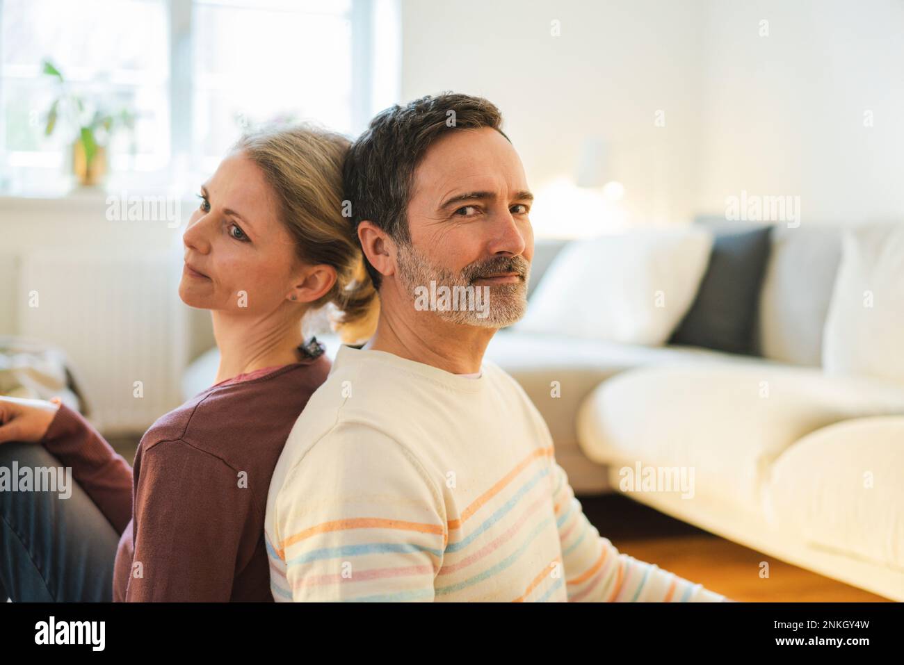 Mature man sitting back to back with wife at home Stock Photo - Alamy