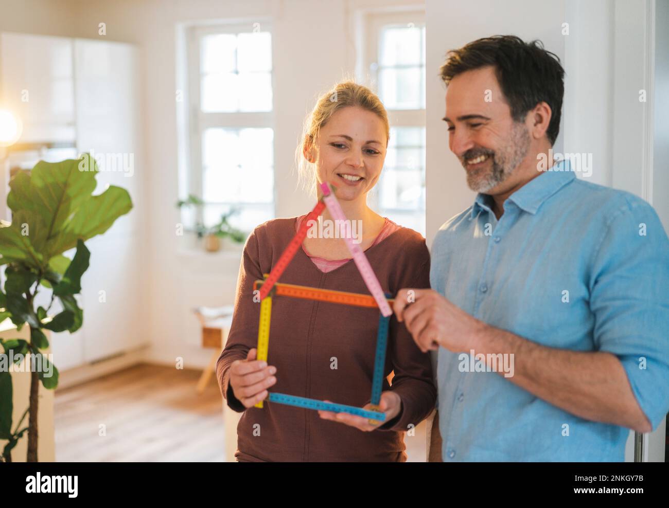Smiling man talking to woman holding house model made of folding ruler ...