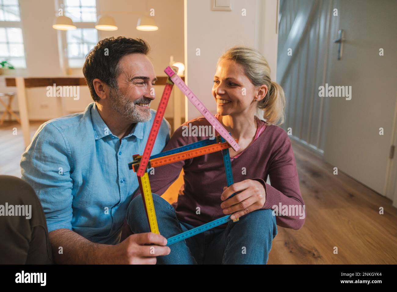 Smiling mature couple holding house model made with folding ruler at ...