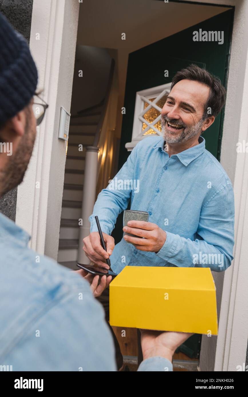Happy customer signing and receiving package from delivery person at ...
