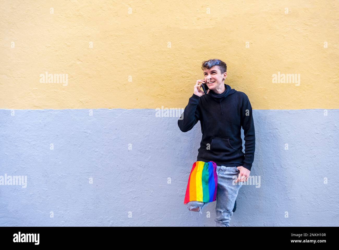 Non binary person with an lgbt rainbow flag talking on the phone outdoors Stock Photo - Alamy
