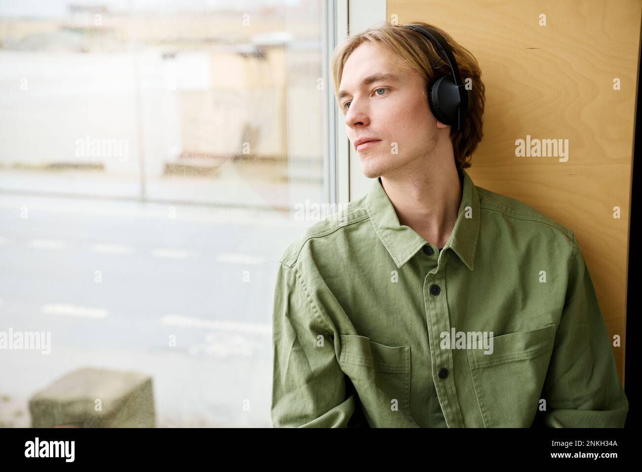 Young man looking out of window wearing bluetooth headphones Stock ...