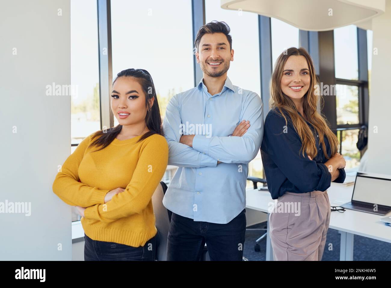 Confident business colleagues with arms crossed standing at workplace ...