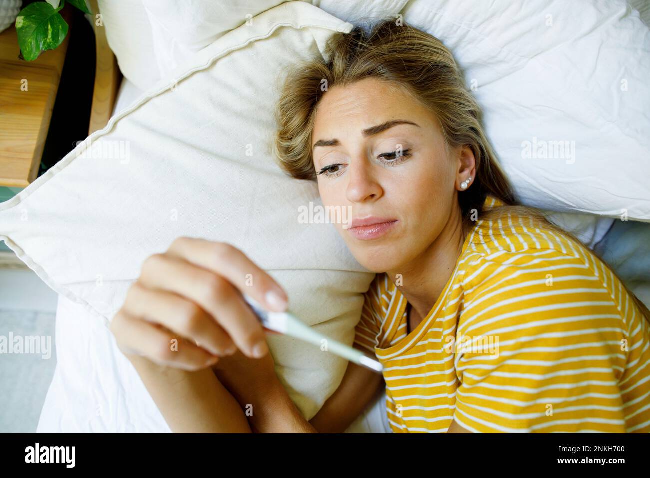 ill woman checking temperature with thermometer in bed at home Stock ...