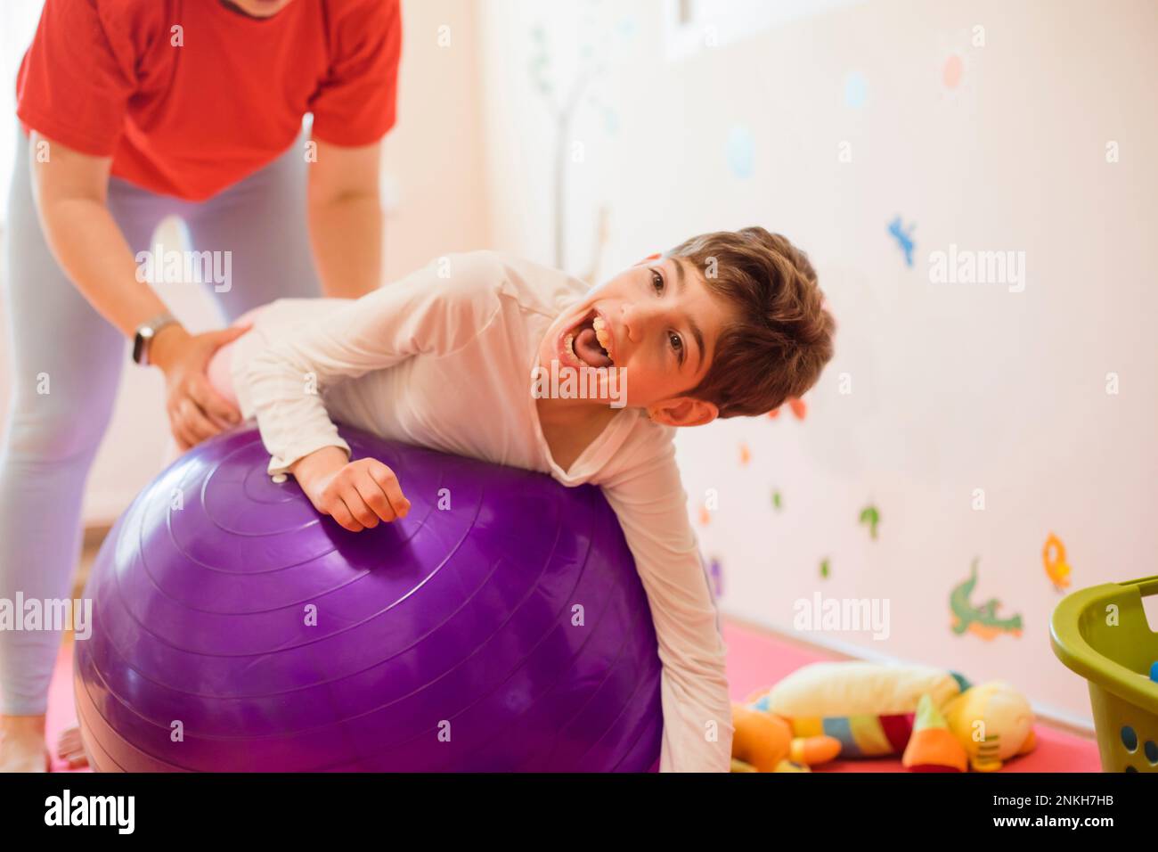 Physical therapist assisting girl with disability lying on fitness ball ...