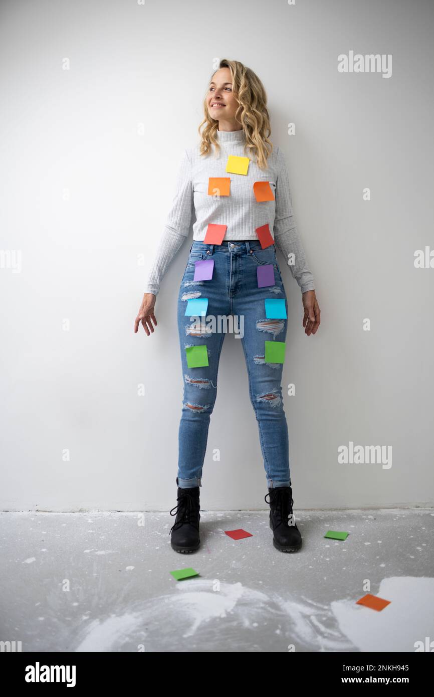 Smiling woman with colorful adhesive notes on body standing in front of ...