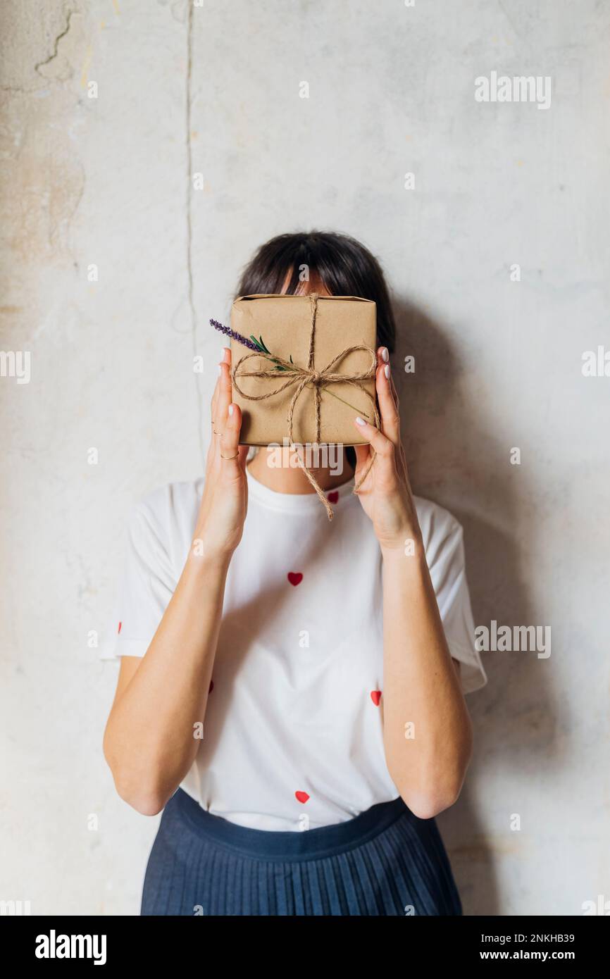 Woman covering face with gift box in front of wall Stock Photo - Alamy