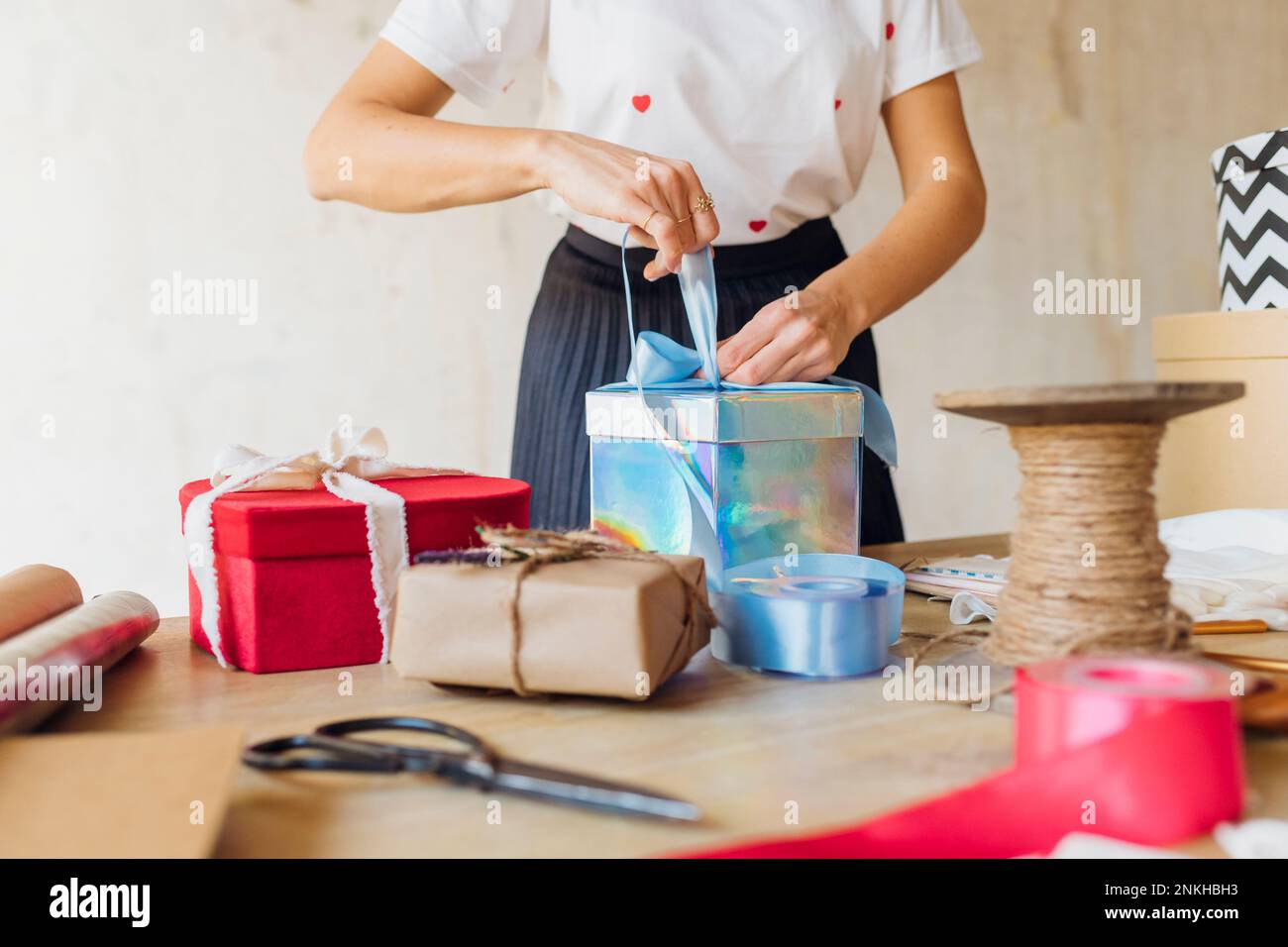Woman tying ribbon on gift box at desk Stock Photo - Alamy