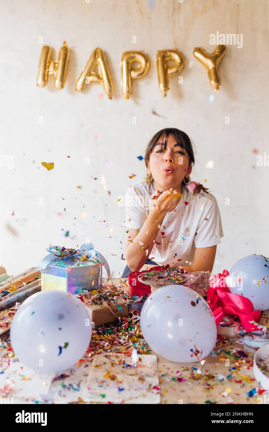 Woman blowing confetti standing in front of wall Stock Photo - Alamy