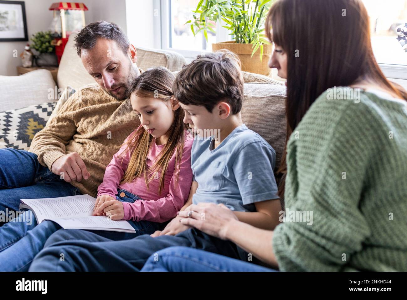 Girl reading book with family in living room at home Stock Photo - Alamy