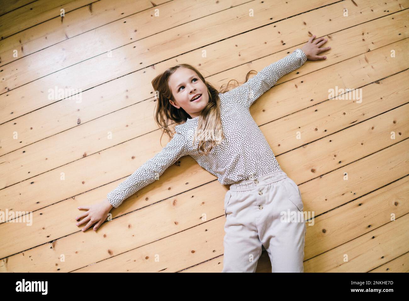 Thoughtful girl with arms outstretched lying on floor at home Stock ...