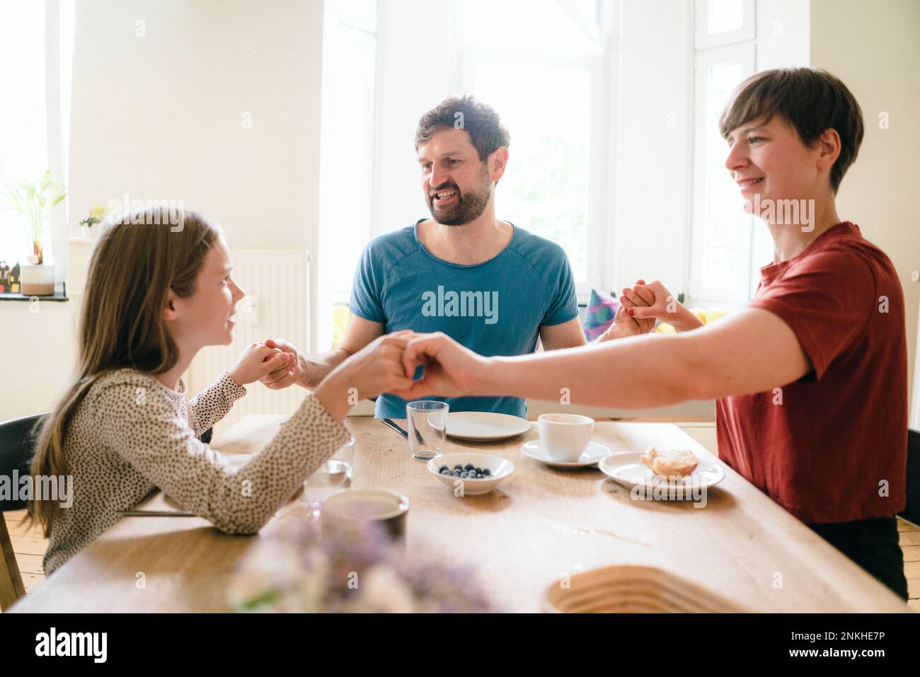 Father and mother holding hands with daughter sitting at dining table ...
