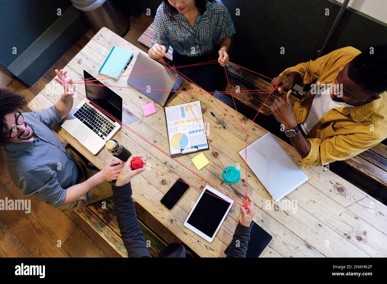 Business colleagues playing cat's cradle sitting at desk in office ...