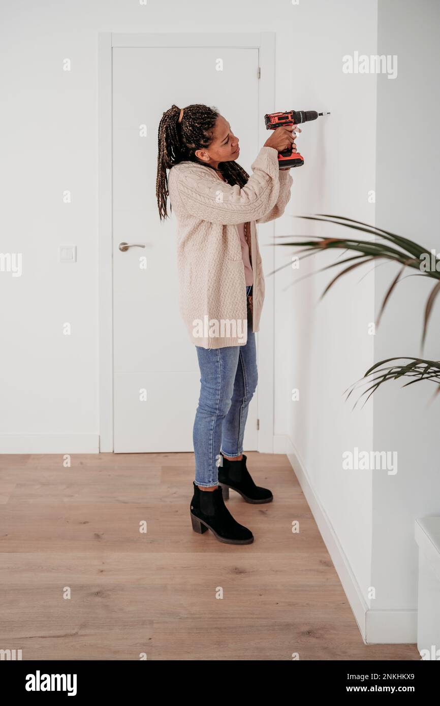 Mature woman using drill machine on wall at home Stock Photo - Alamy