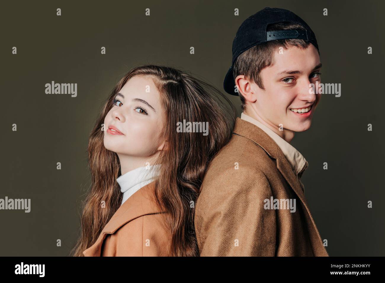 Happy teenage boy and girl standing back to back against gray ...