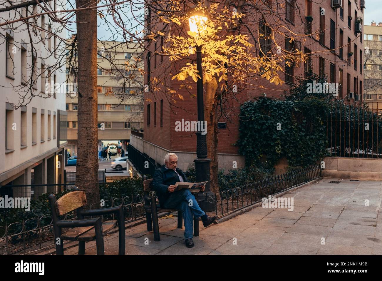 Senior man reading book sitting near lamp post Stock Photo - Alamy