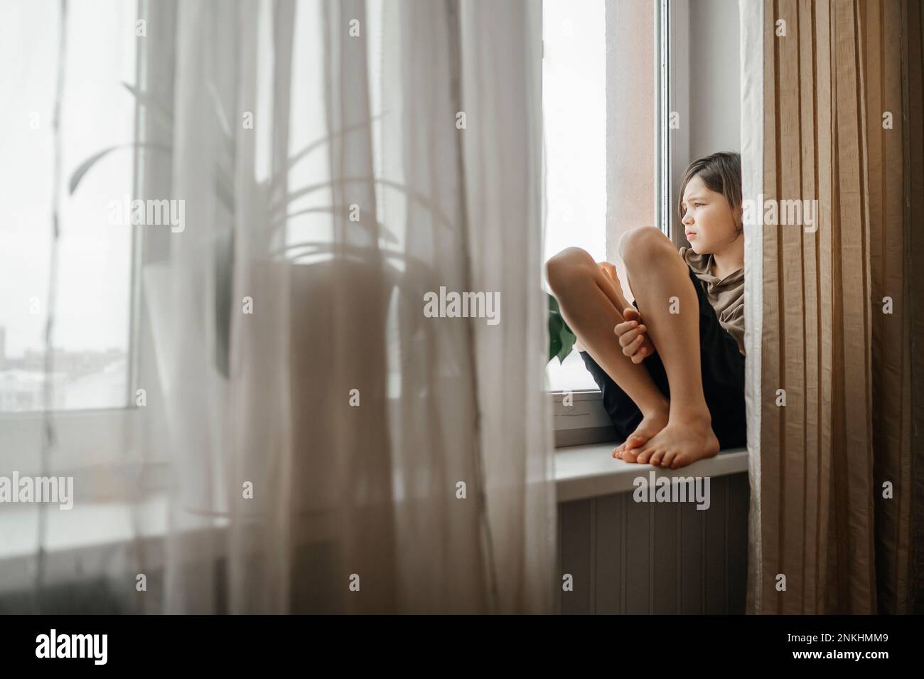 Sad boy sitting on window sill at home Stock Photo - Alamy