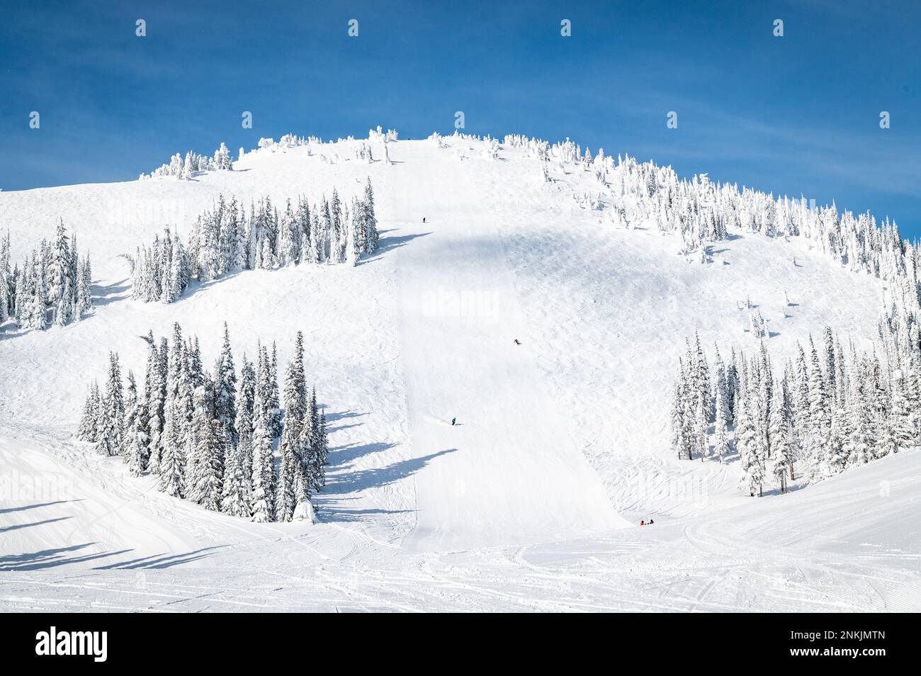 Photo of 3 skiers heading down a widely groomed trail on the mountain ...