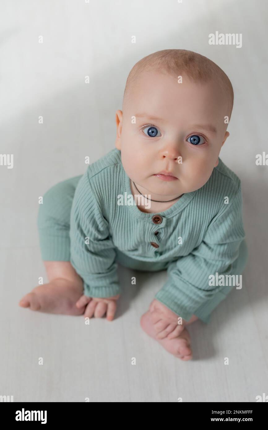 portrait of a charming chubby baby in a green jumpsuit sitting on the ...