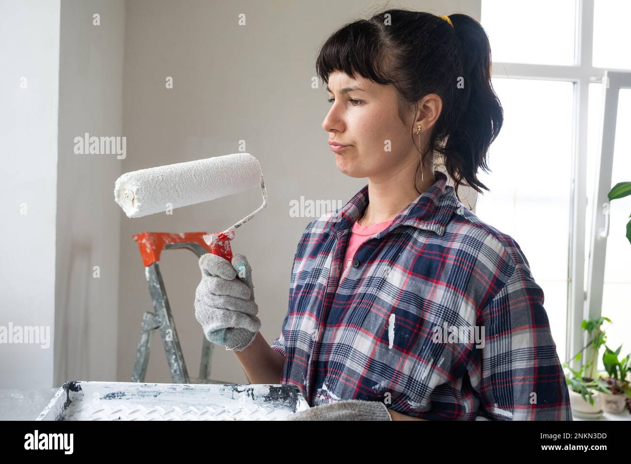 puzzled woman in paint roller and white paint for walls in hands close ...