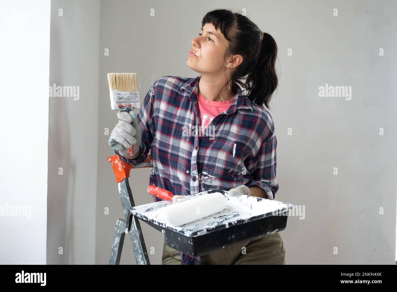 puzzled woman in paint roller and white paint for walls in hands close ...