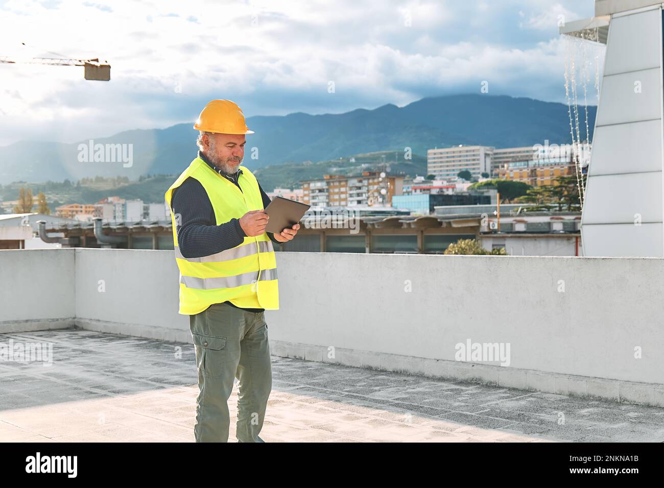 Middle aged bearded supervisor in hardhat and safety vest with tablet ...