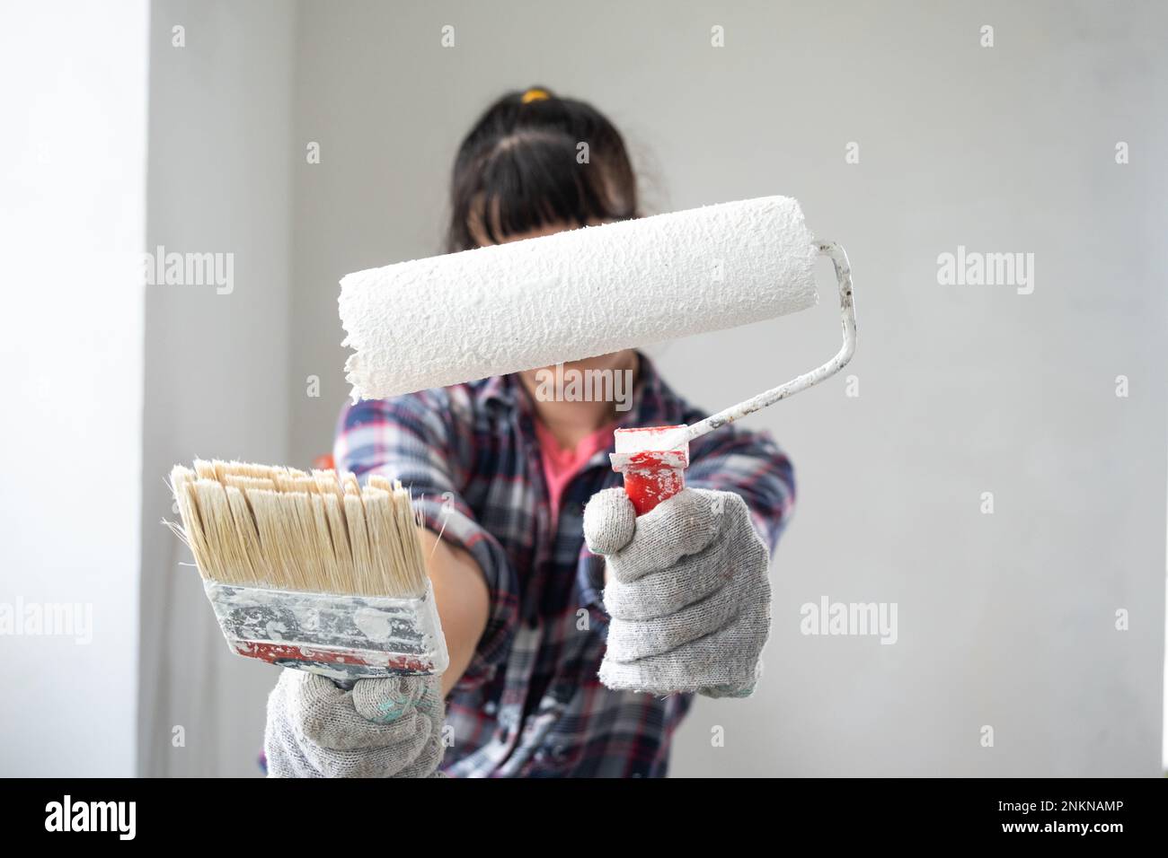 puzzled woman in paint roller and white paint for walls in hands close ...