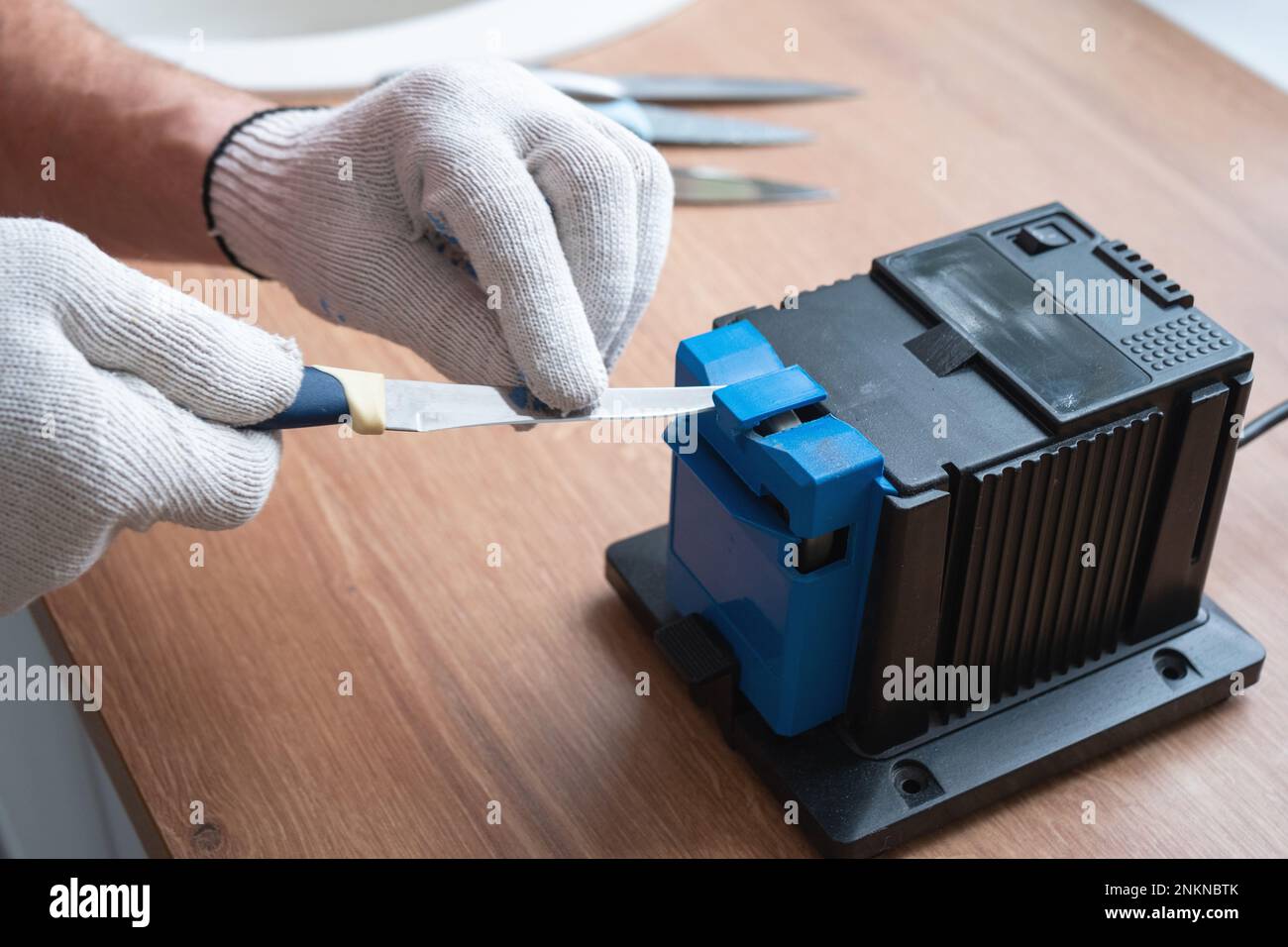 Sharpening a knife on an electric sharpener at home. The man's hand ...