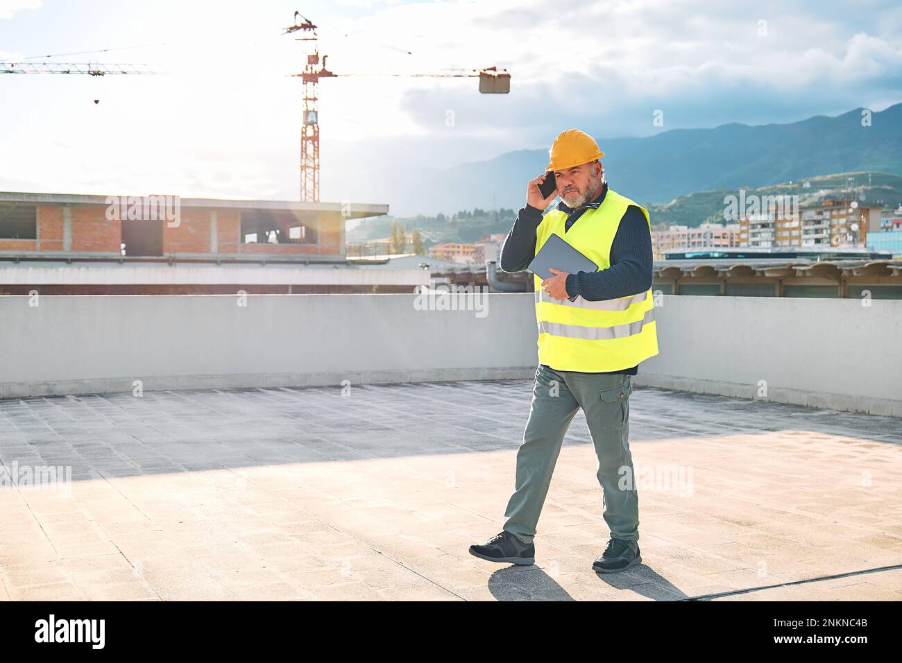 Middle aged bearded supervisor in hardhat and safety vest with tablet ...
