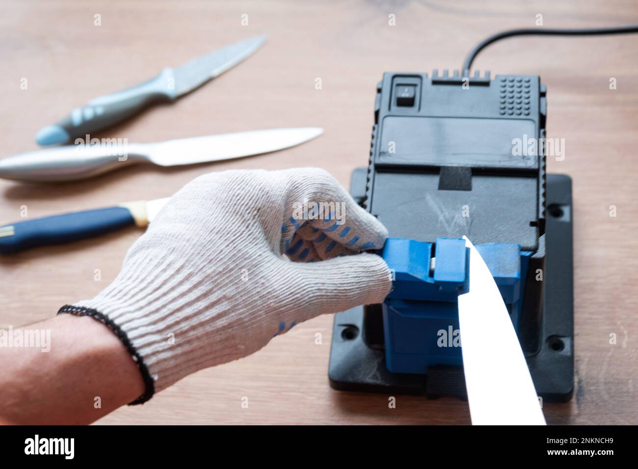 Sharpening a knife on an electric sharpener at home. The man's hand ...