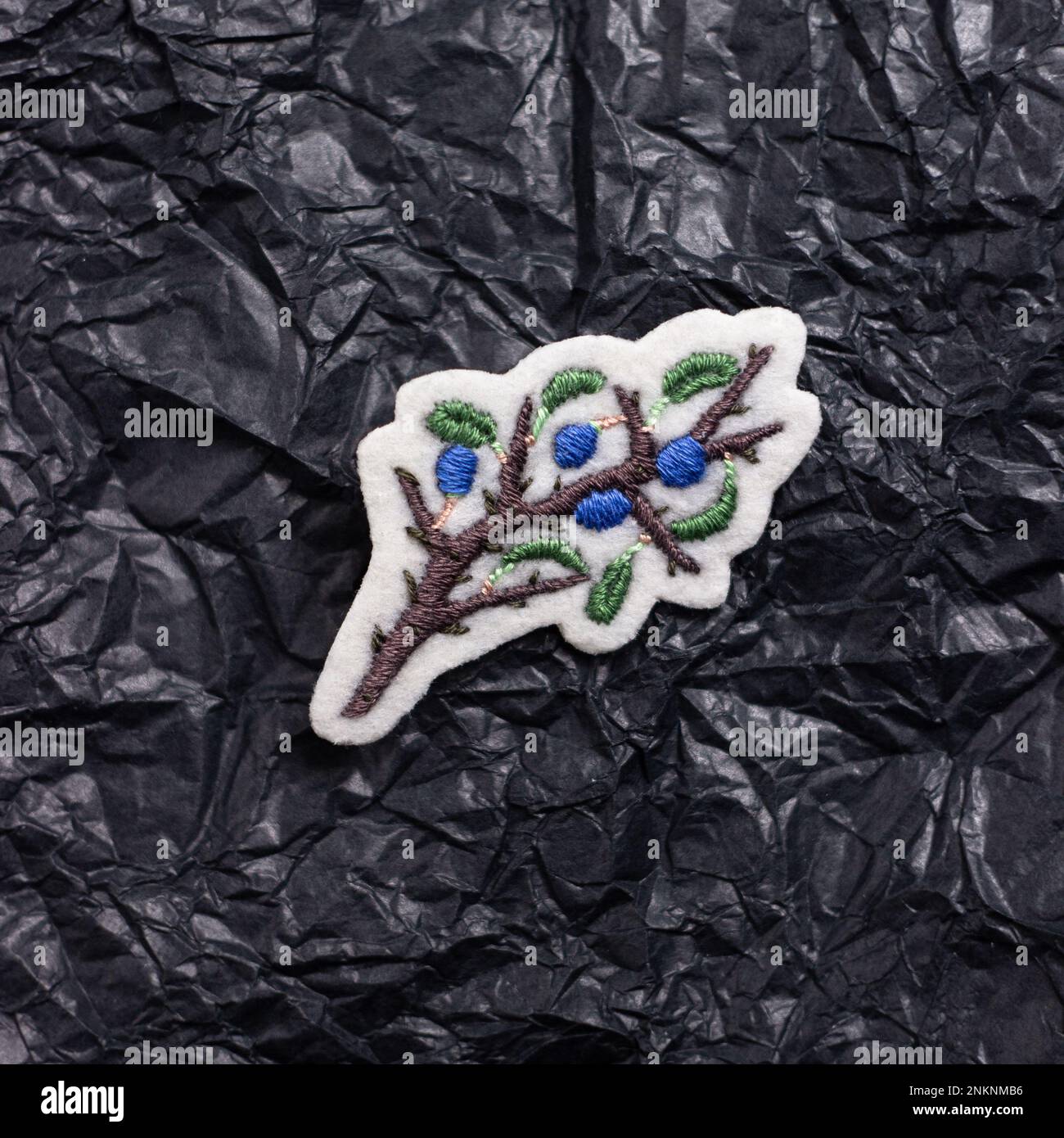 A brooch embroidered with threads on white felt in the form of a ...