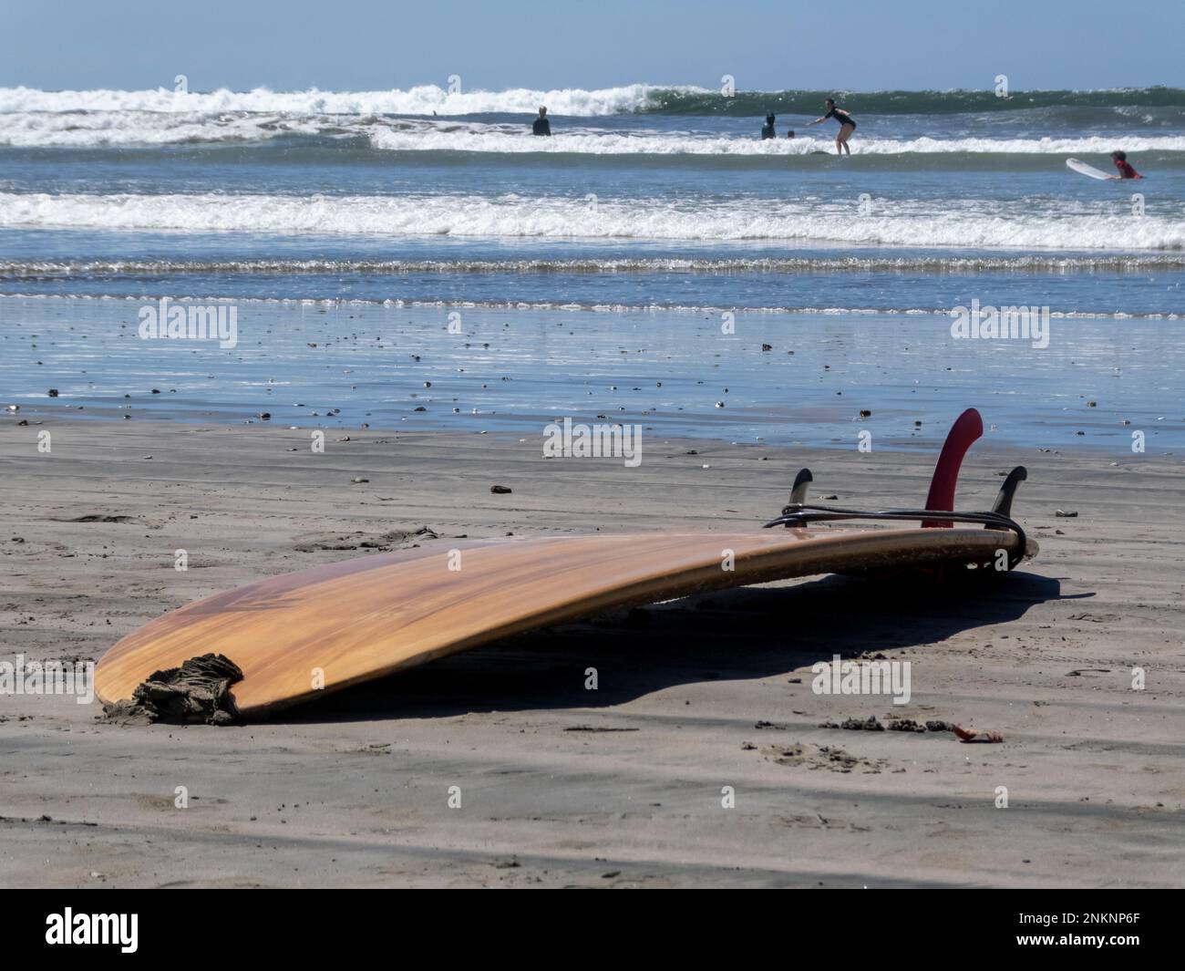 A surfboard rests on the beach while surfers ride waves in the ...