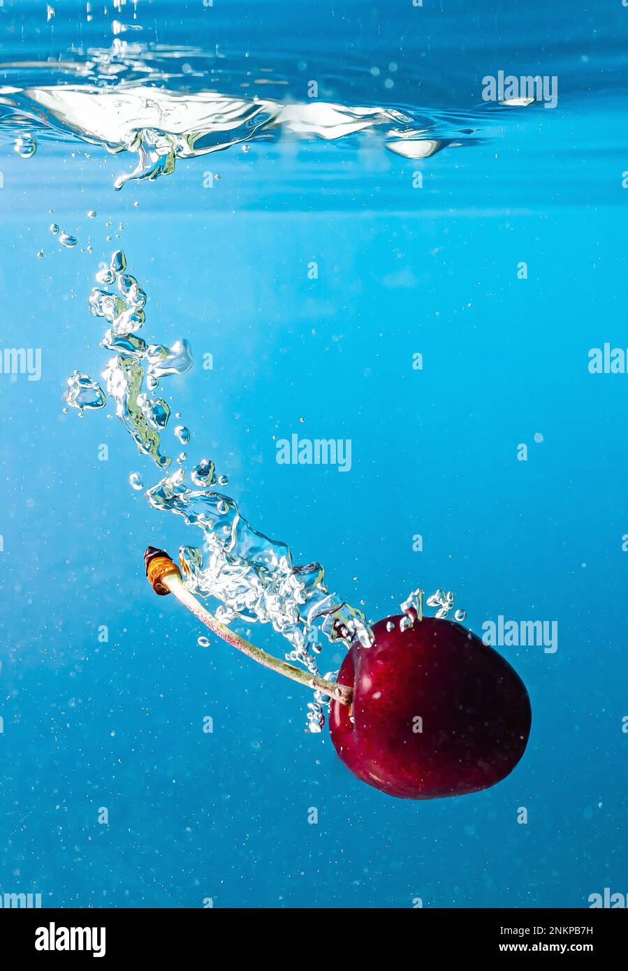ripe cherries fall into the water raising splashes and air bubbles ...