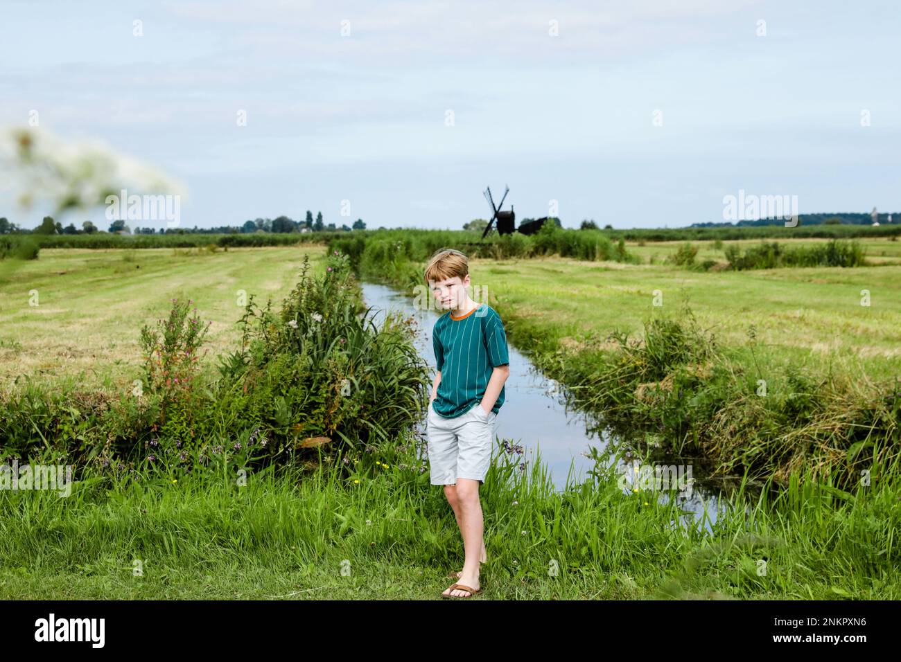 Boy standing by small canal with windmill in distance Stock Photo - Alamy