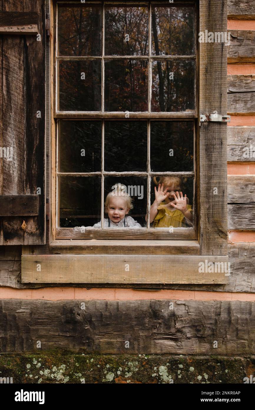 Two children looking through window of wooden hut towards camera Stock ...