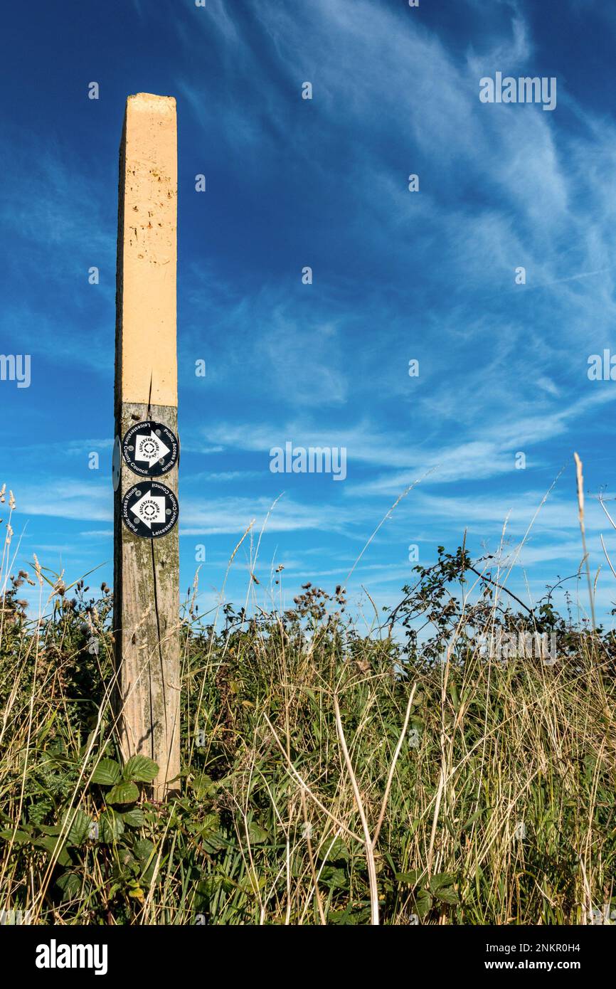 Yellow painted wooden footpath marker post against blue sky with ...