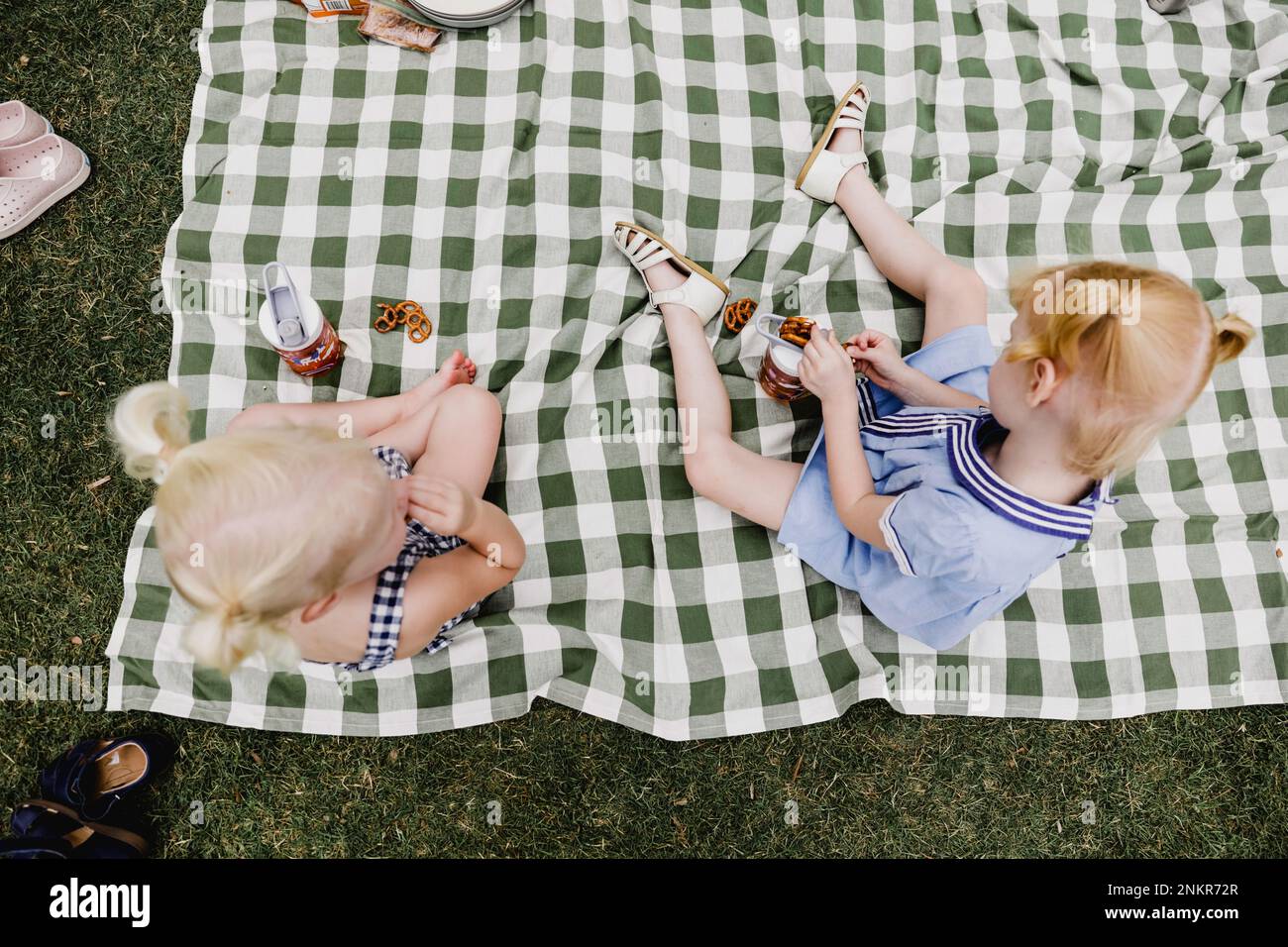 Two girls sitting on gingham picnic rug eating food Stock Photo - Alamy
