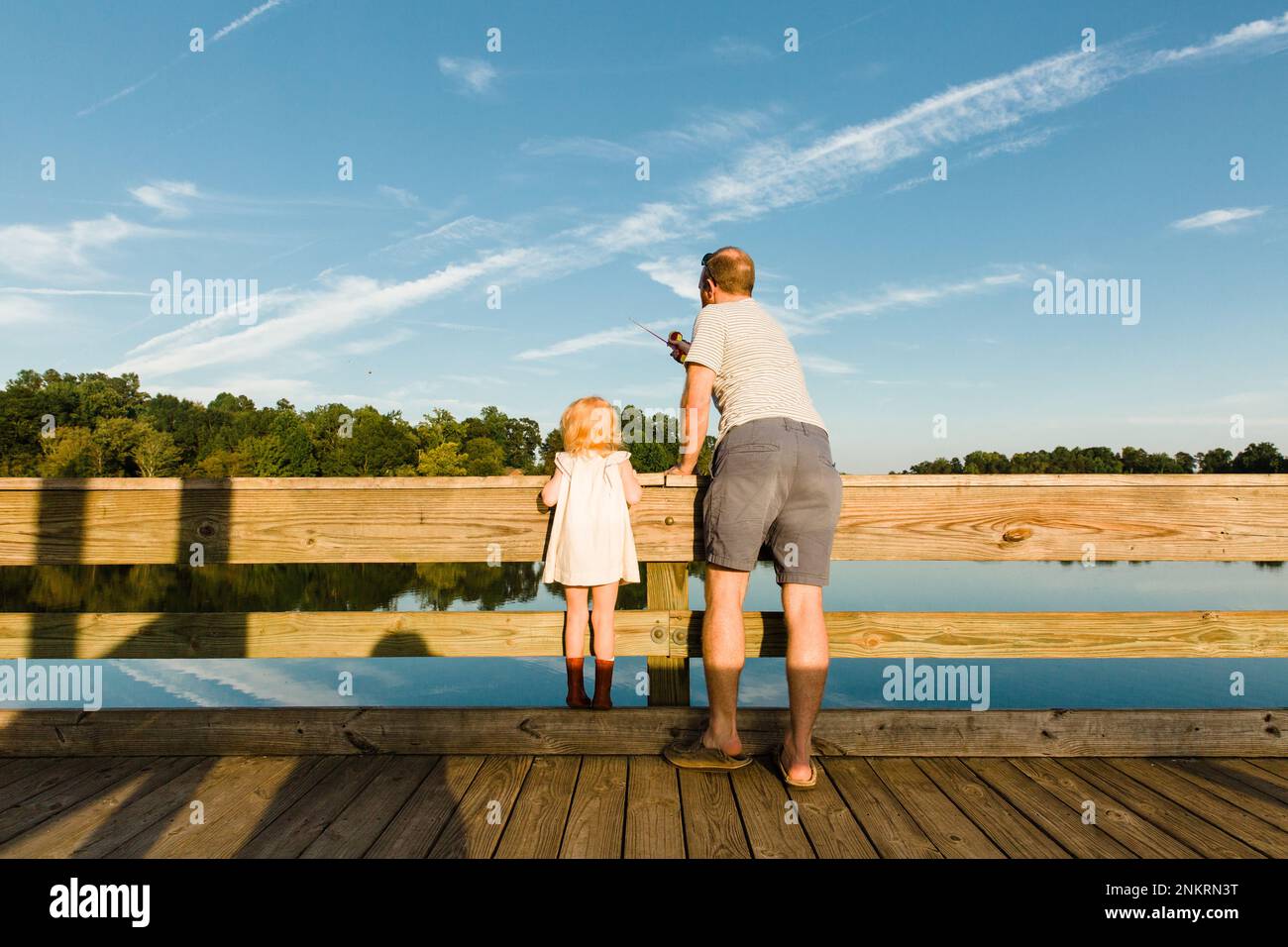 Father and daughter leaning over wooden fence fishing, with view of ...