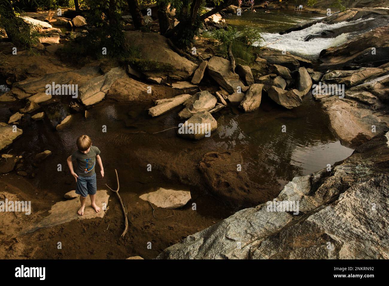 High angle of young boy playing in stream, standing on rock Stock Photo ...