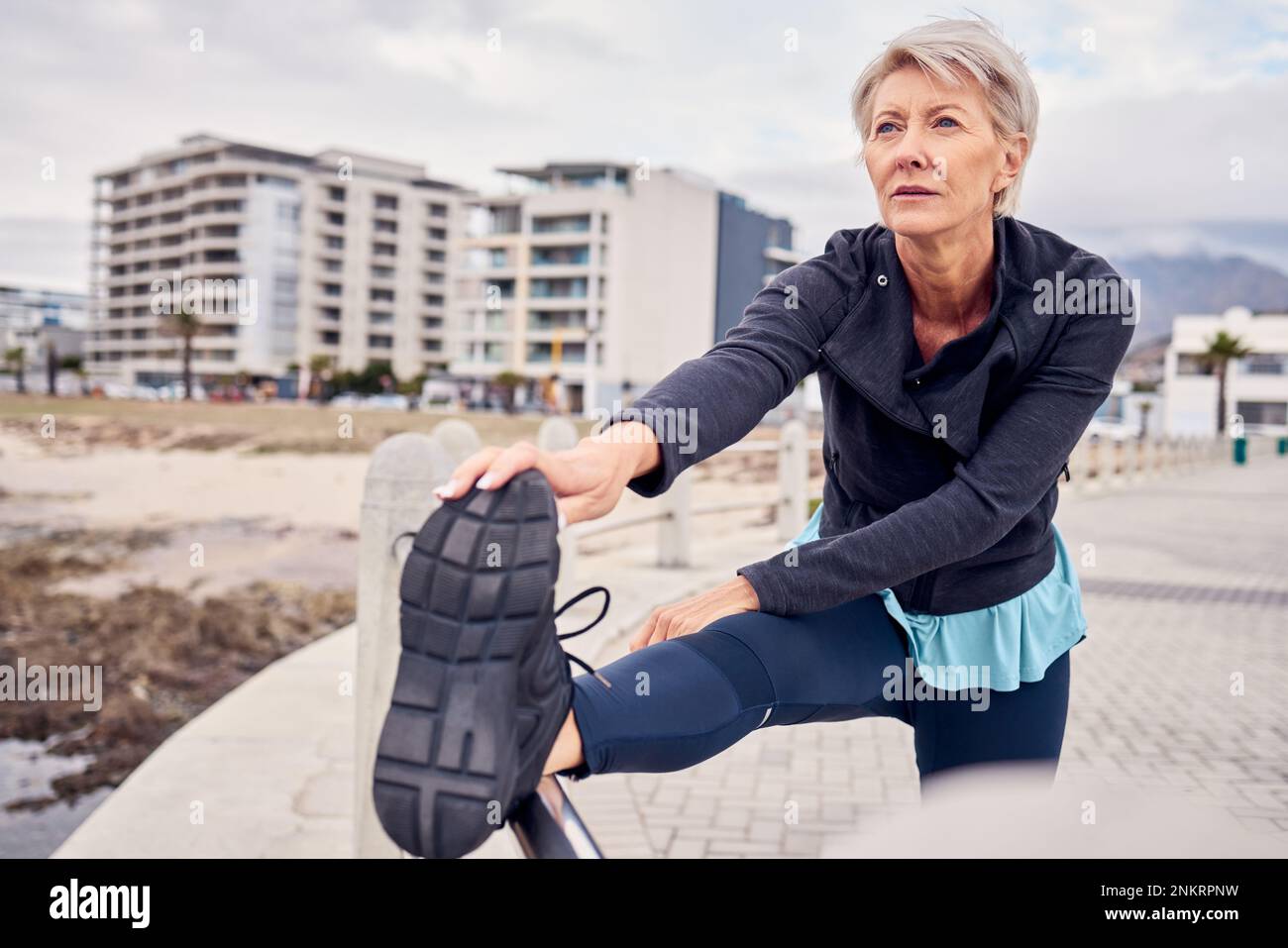 Woman, serious and stretching legs outdoor at beach sidewalk for energy ...