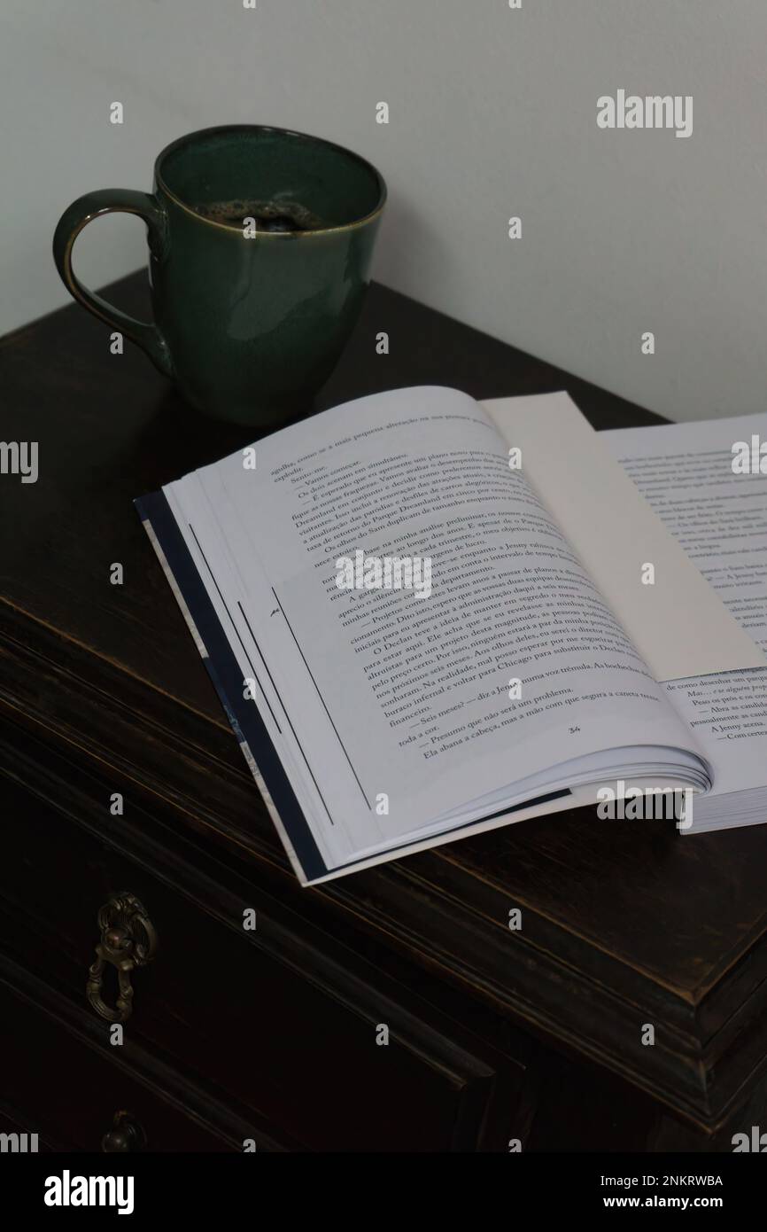 Open book and coffee cup on antique bedside table Stock Photo - Alamy