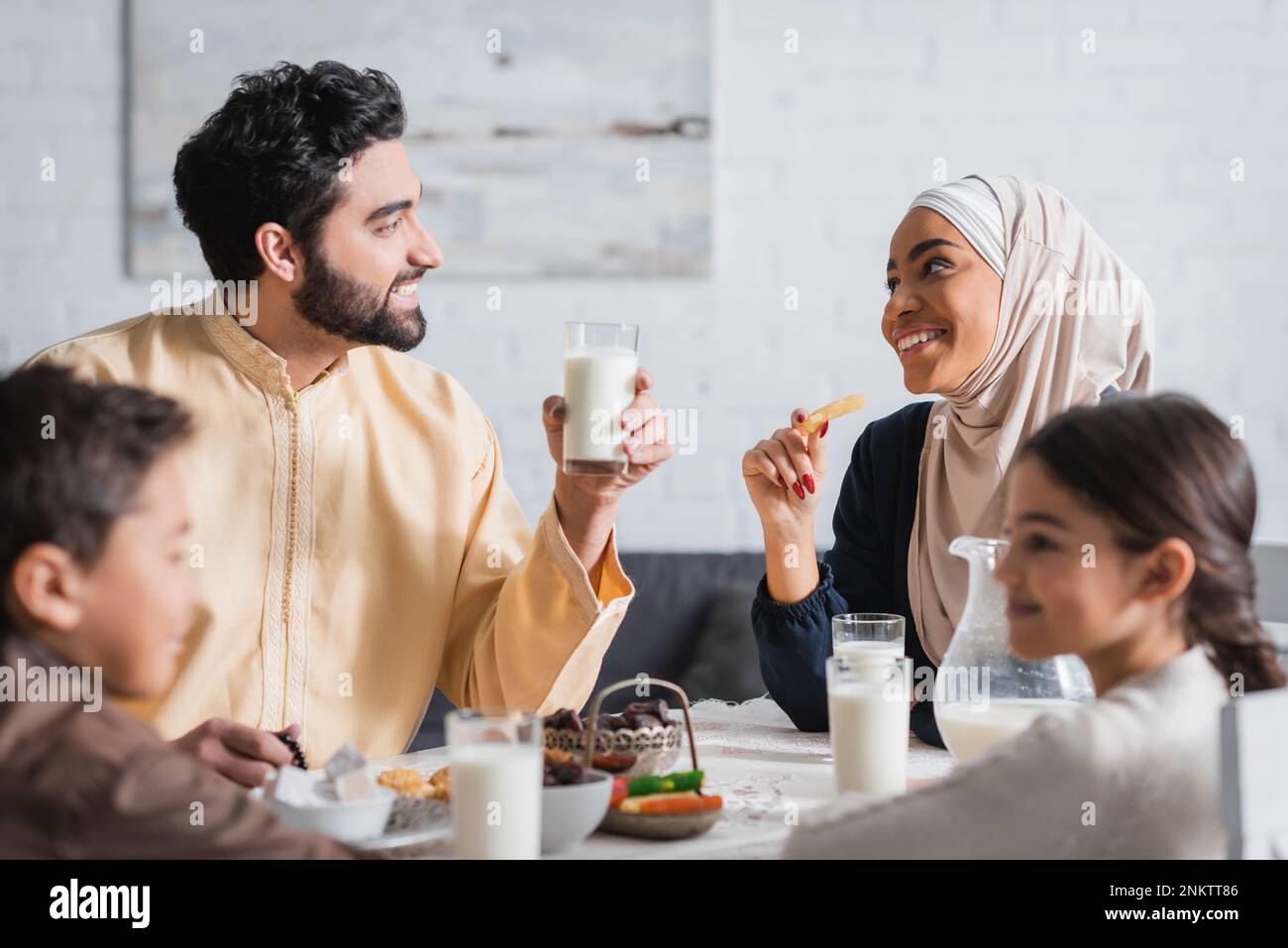 happy muslim parents looking at each other near blurred kids and suhur ...