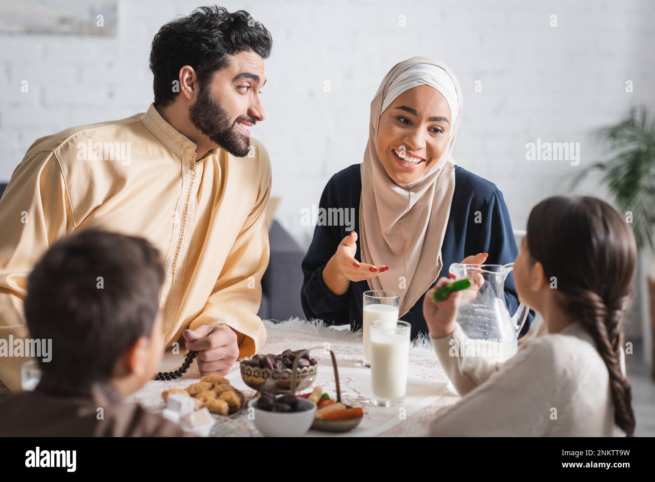 Positive muslim family talking to kids during suhur breakfast at home ...