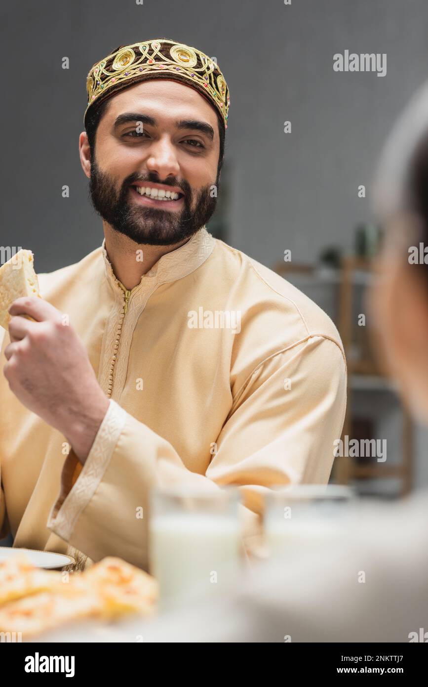 Smiling muslim father holding pita bread near blurred daughter at home ...